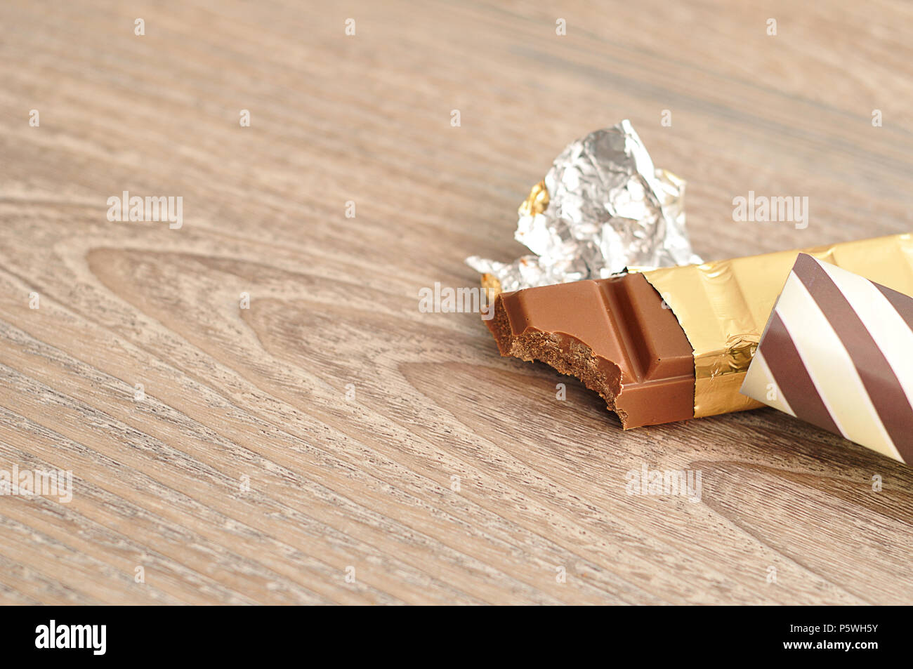 A candy bar unwrapped and a bite taken out of it wooden background ...