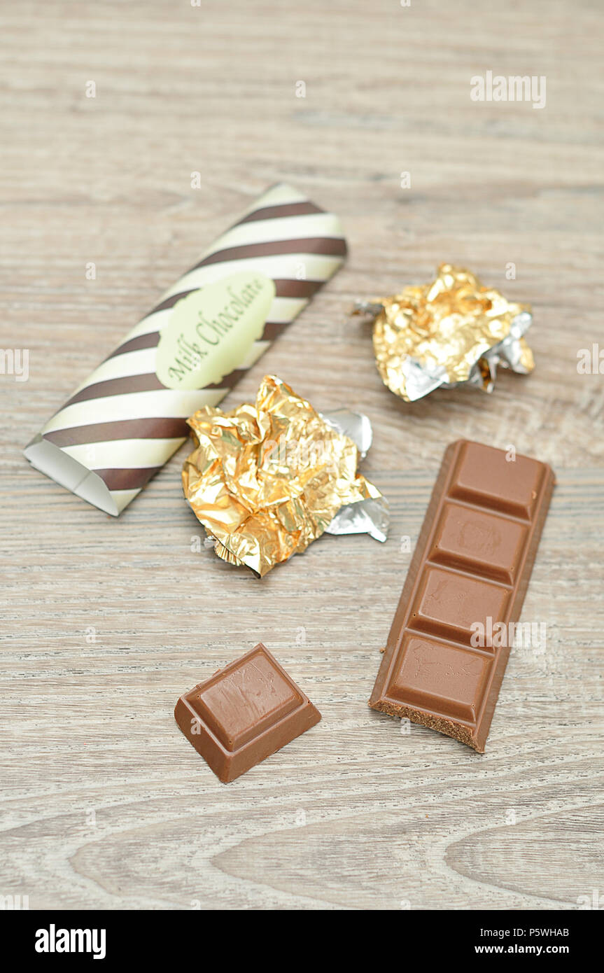 A chocolate candy bar with a piece broken off with the wrappers out of ...