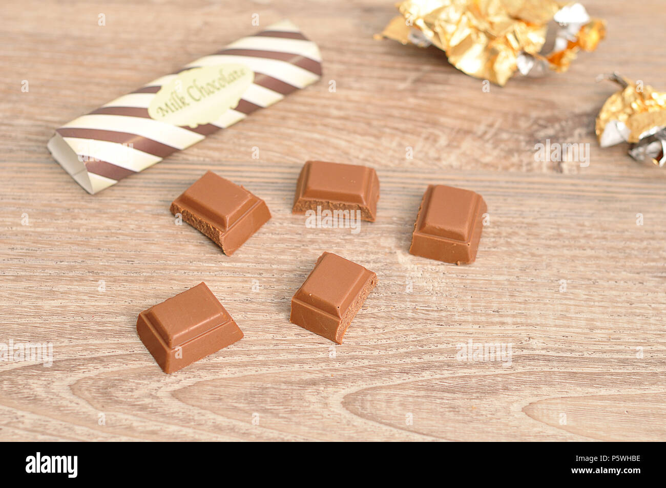 A chocolate candy bar broken into pieces with the wrappers out of focus ...