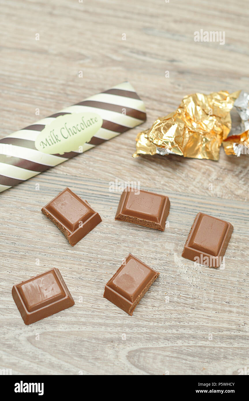 A chocolate candy bar broken into pieces with the wrappers out of focus ...