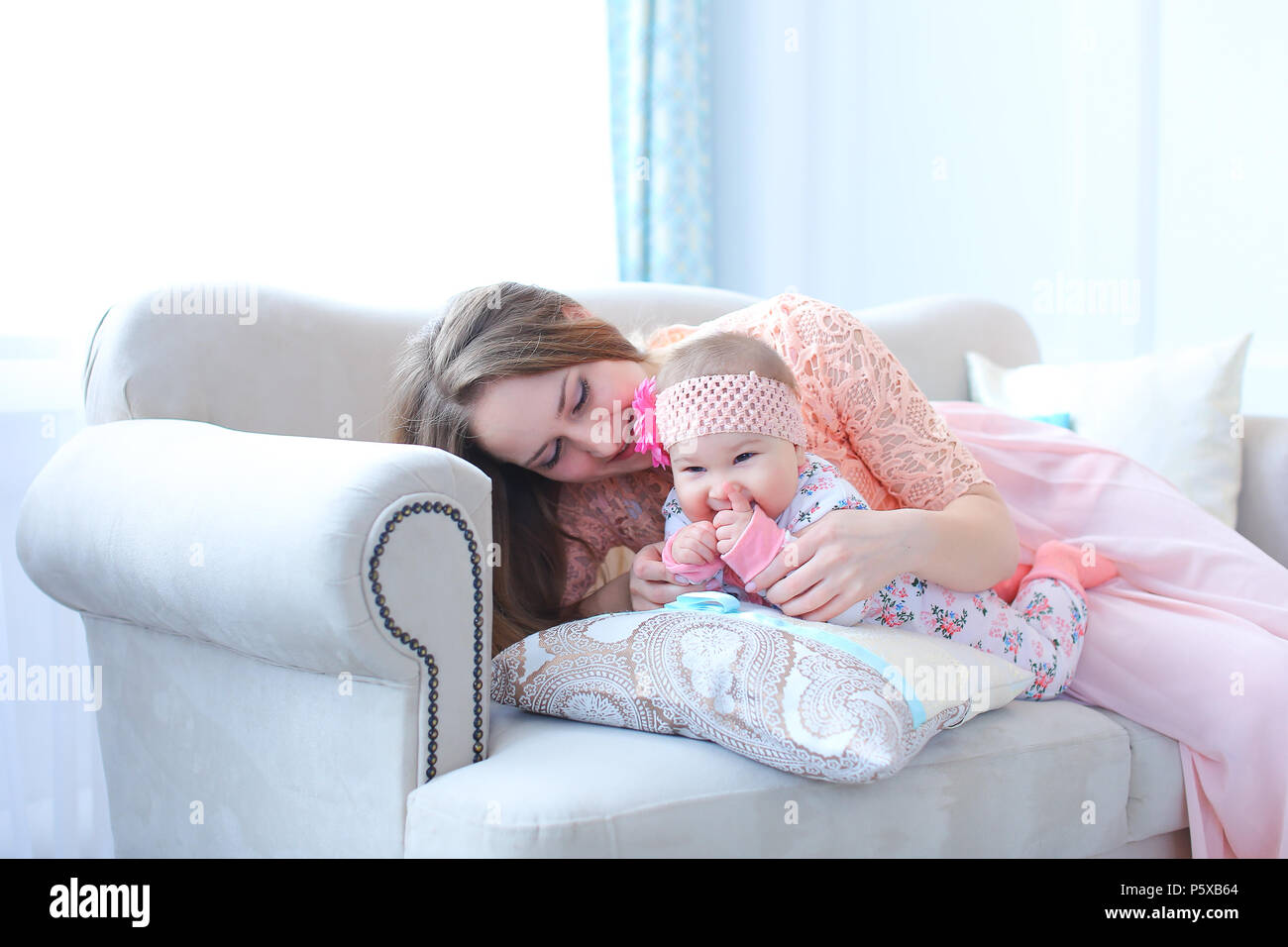 Young pretty mother sitting with child on sofa and wearing pink dress ...