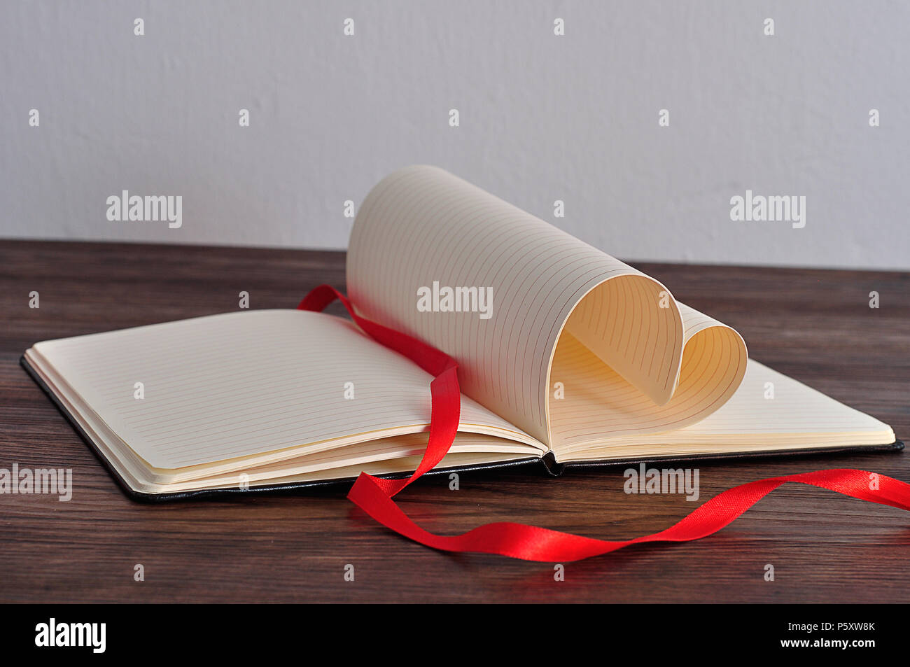 Pages of a book bend in a heart shape displayed with a red ribbon Stock ...
