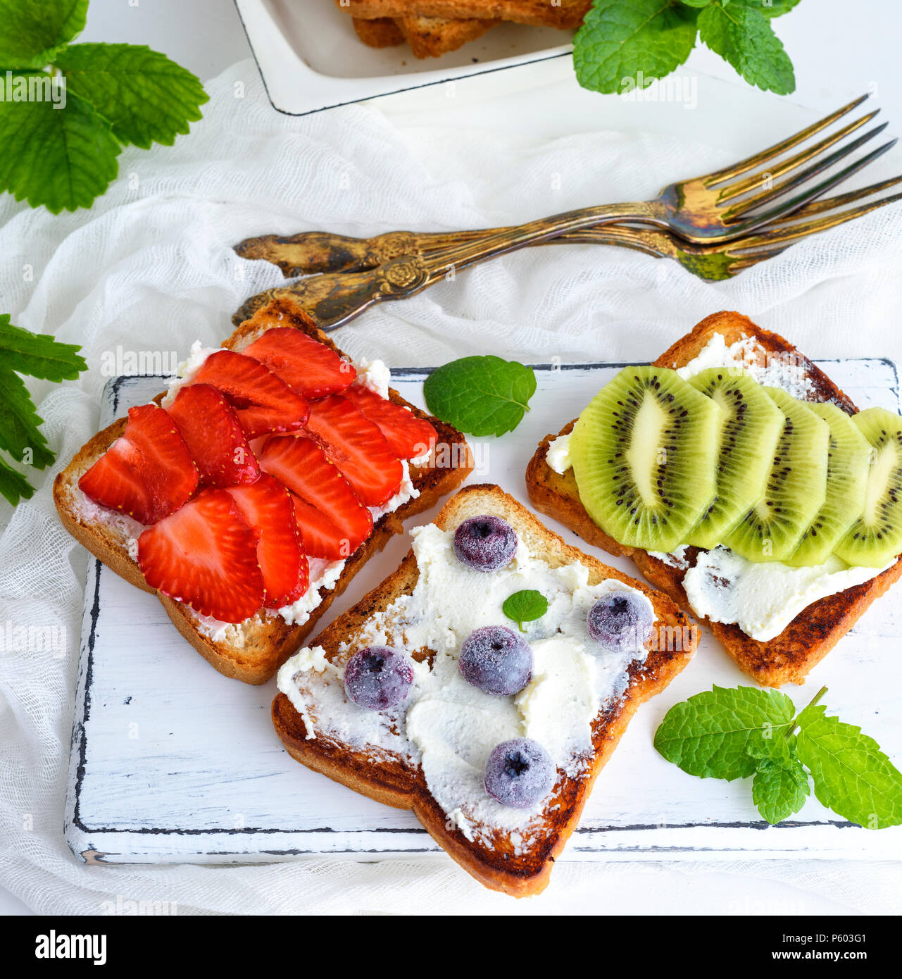 three French toasts with soft curd and fruit on a white wooden board ...