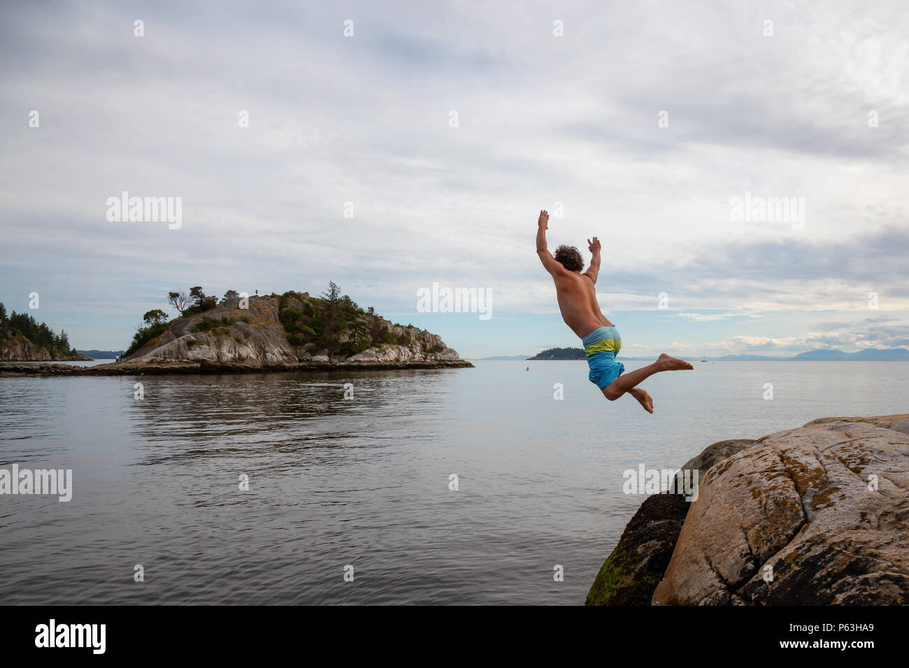 Adventurous man is cliff jumping from a rock into the ocean. Taken in ...