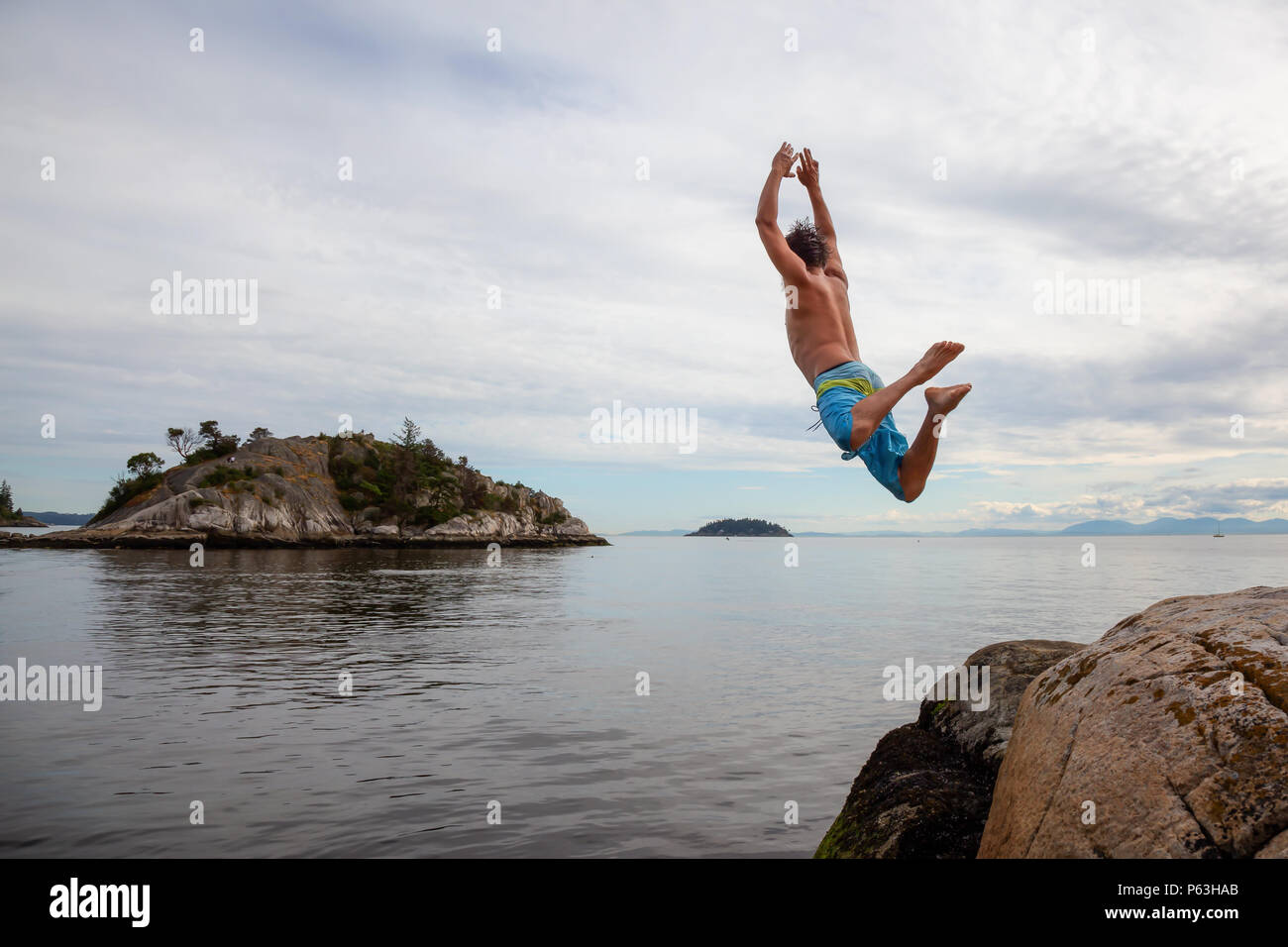 Adventurous man is cliff jumping from a rock into the ocean. Taken in ...