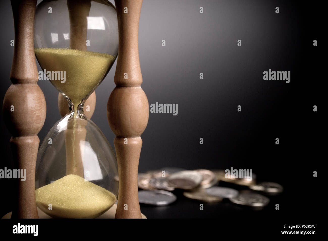 sand clock and coins on black background Stock Photo - Alamy