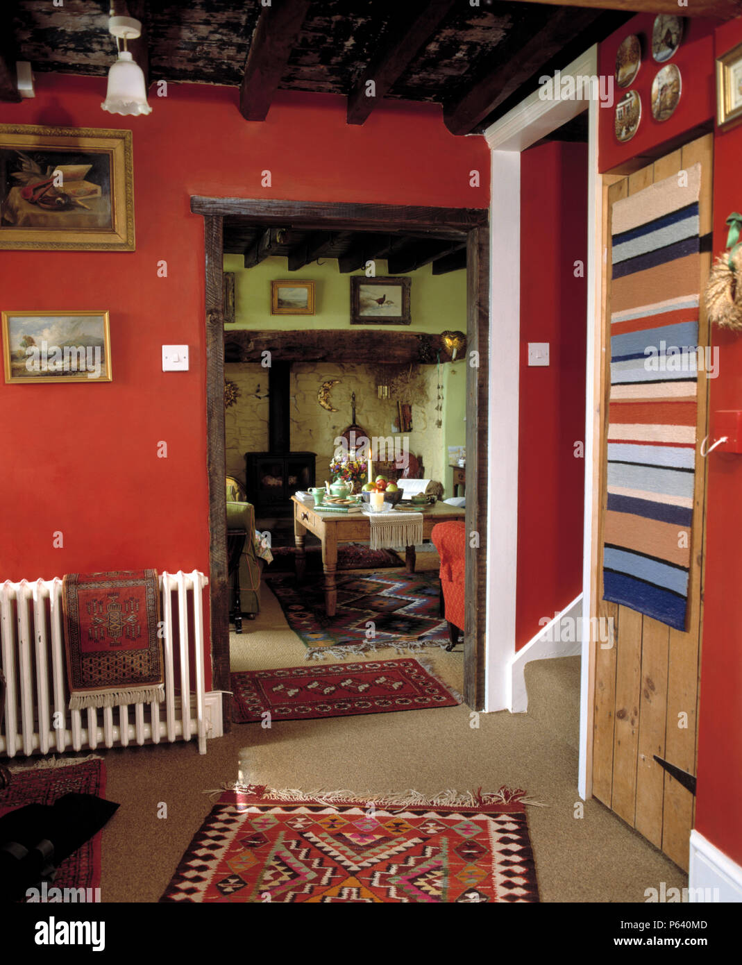 Rugs on radiator and pine door in red cottage hall with view of living ...