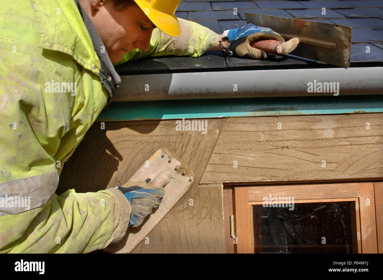 A plasterer rendering a roughcast finish around new hardwood casement ...