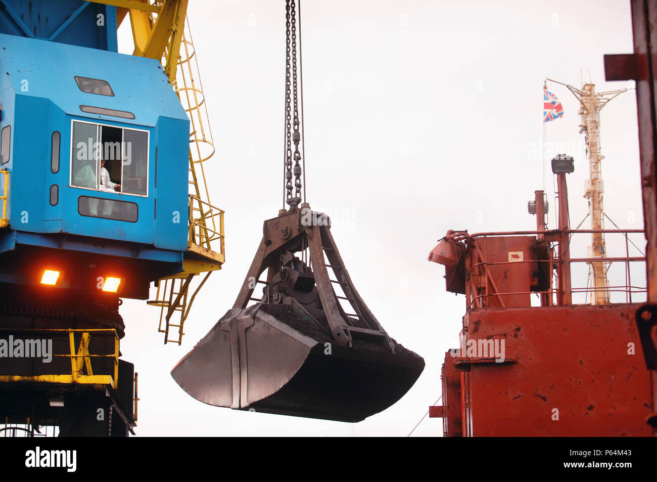 Crane unloading coal from a container ship on the dockside at a port in ...
