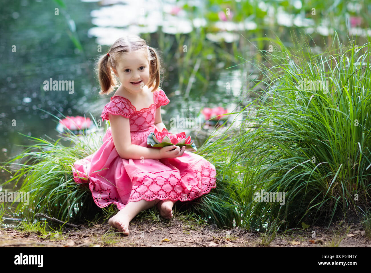 Child sitting at lake shore watching water lily flowers. Little girl ...