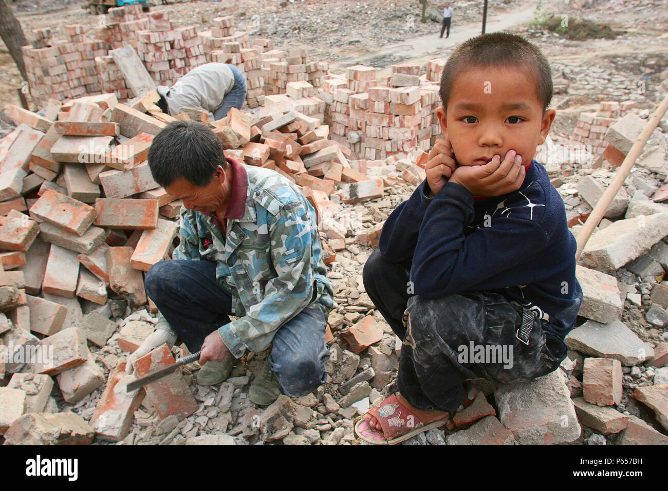 A child sits by his migrant workers parents, as they sift bricks during ...