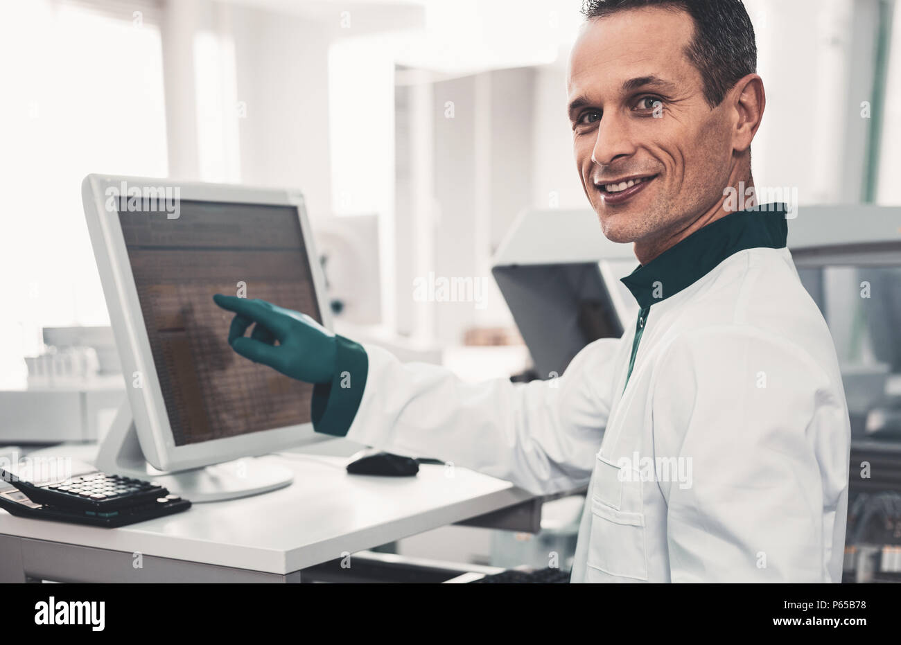Portrait of pleased laboratory assistant pointing at computer screen ...