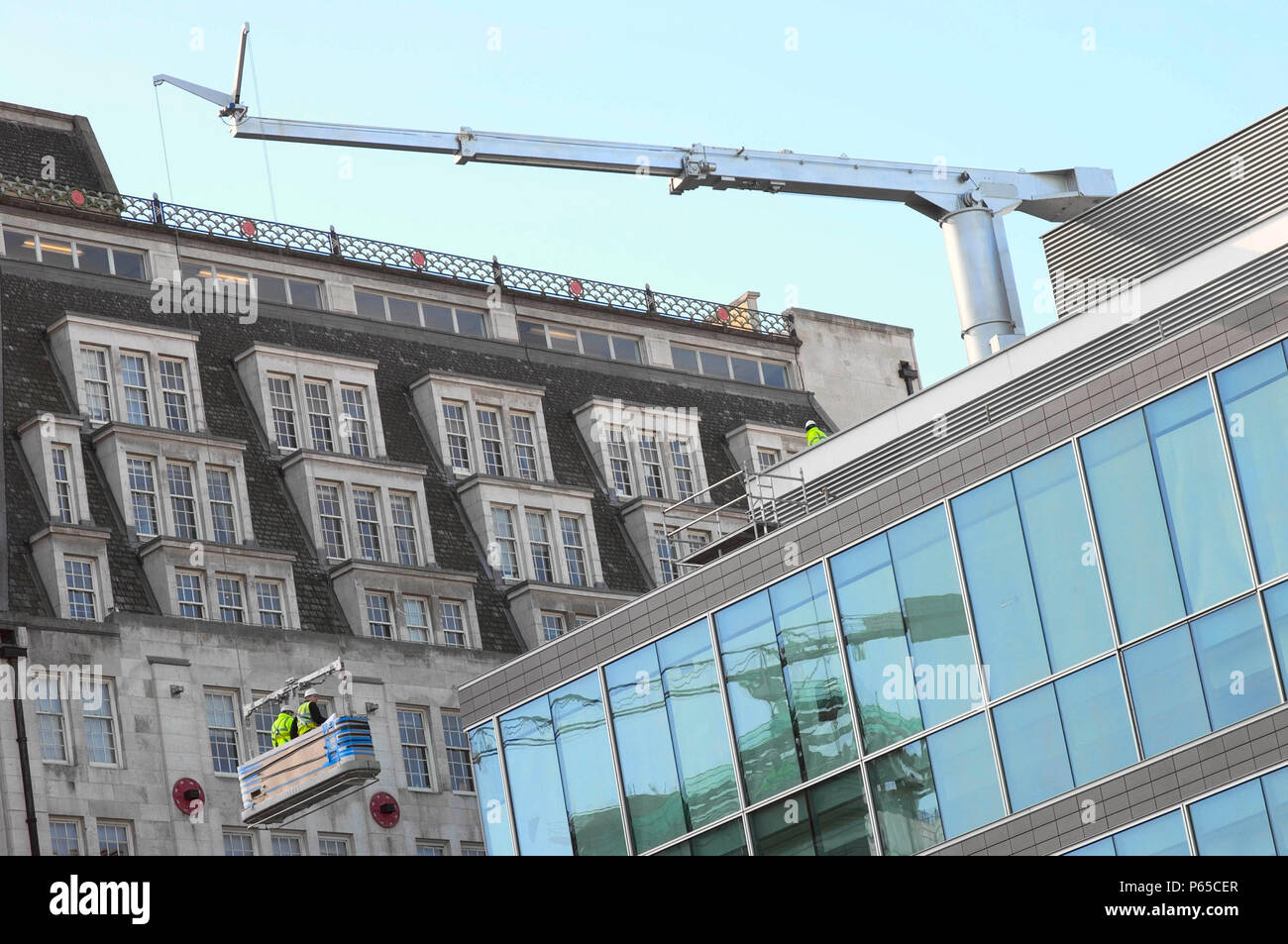 Workmen using newly installed window cleaners cradle installed on a new ...