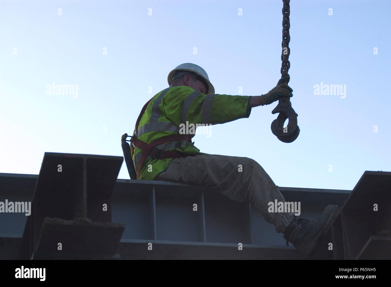 Silhouette of a construction worker in safety equipment securing a hook ...