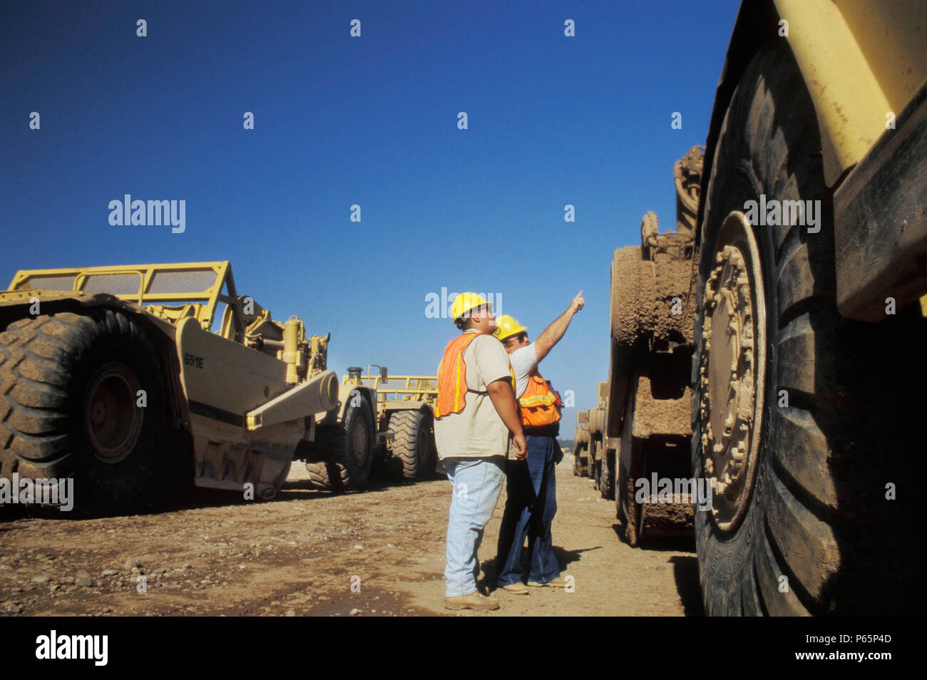 Operator and apprentice checking row of scrapers, huge residential ...