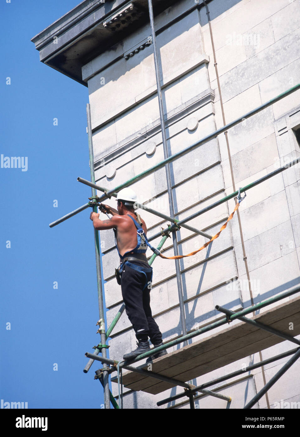 Scaffolder erecting independent scaffolding against face of stone wall ...