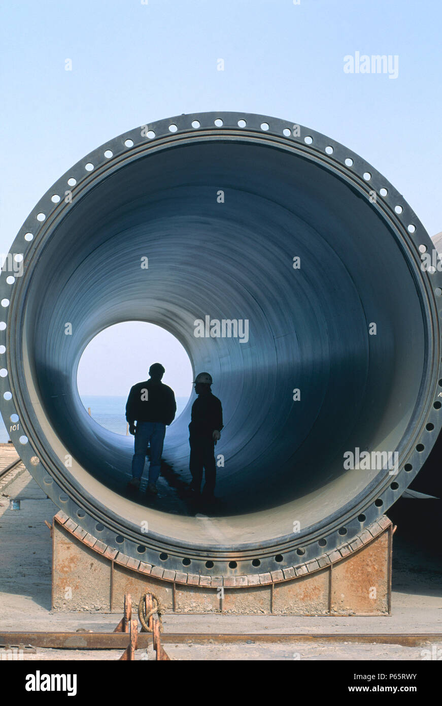 Site workers standing in section of precast concrete water pipe in ...