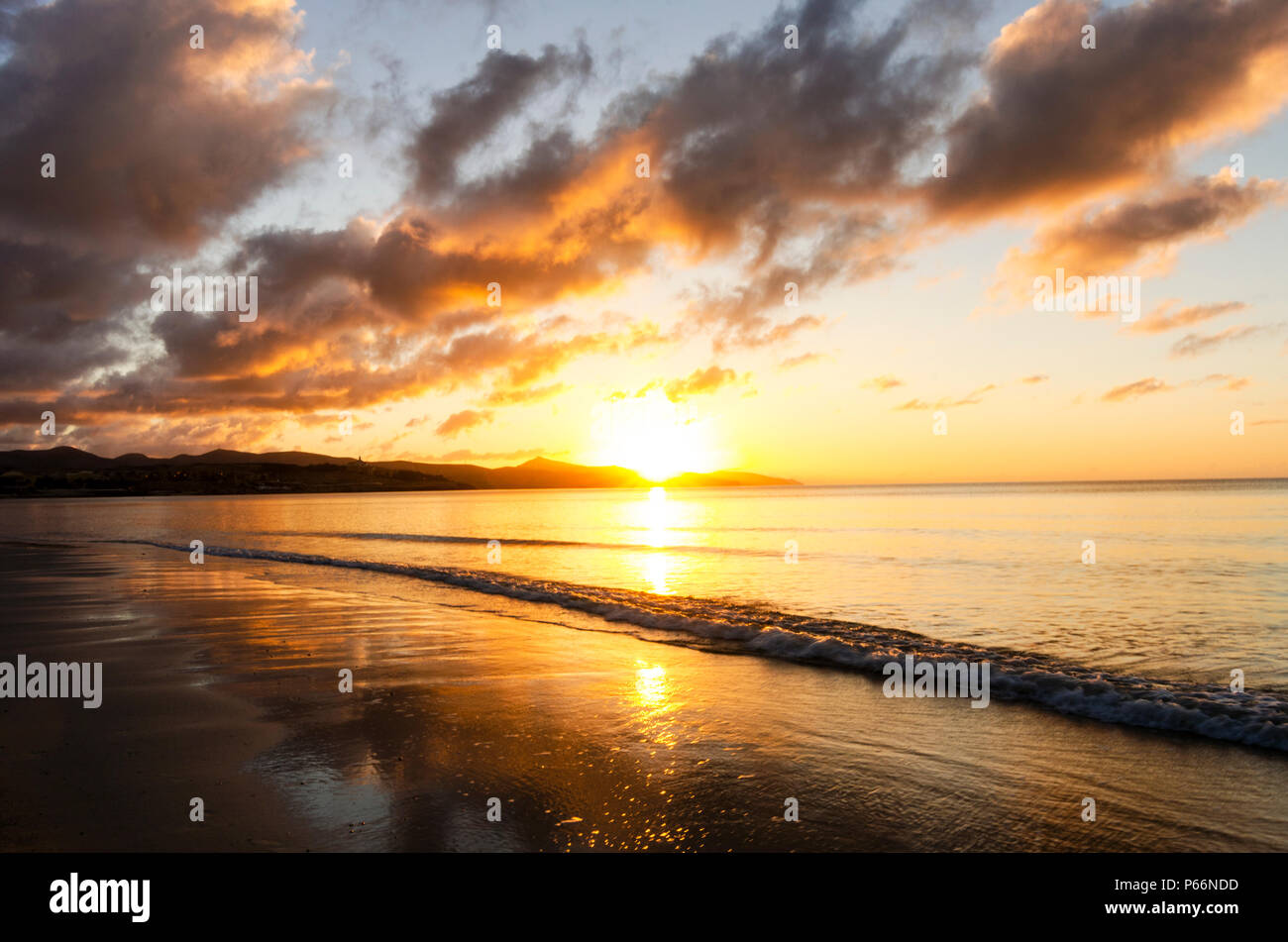 Yellow and orange sunrise on the beach with sun reflection on the wet ...