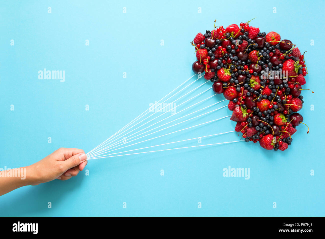 Hand holding balloons made of berries on blue paper background. Healthy ...