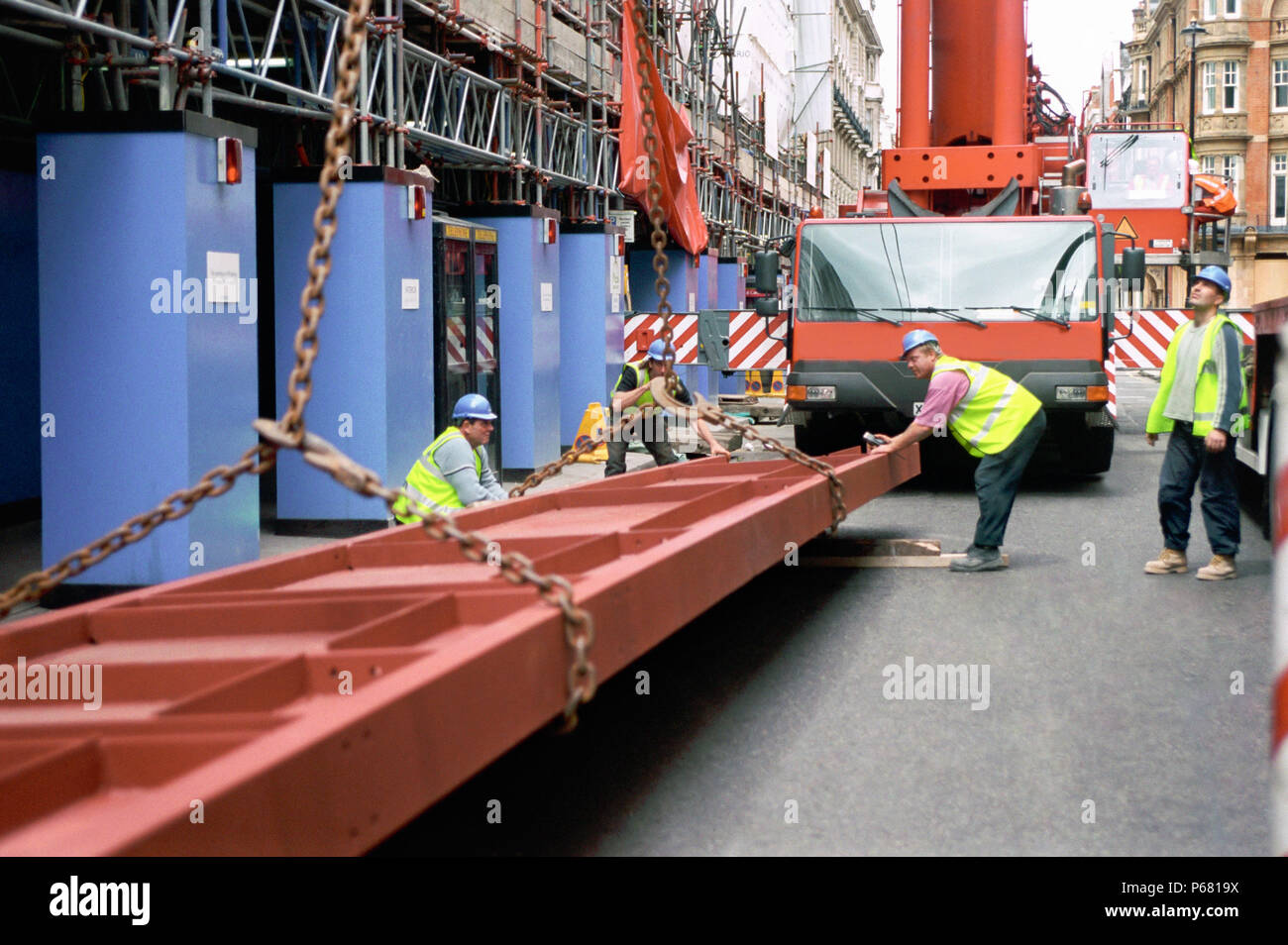 Workmen guiding tower crane lifting steel girder Stock Photo - Alamy