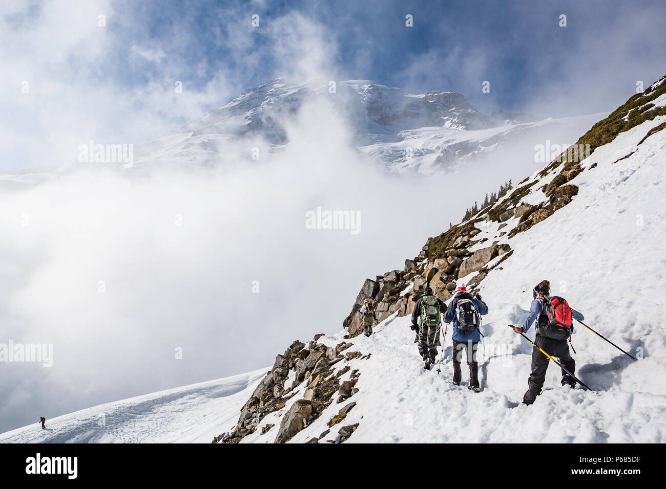 The summit of Mt Rainier looms above clouds. Climbers and hikers on the ...