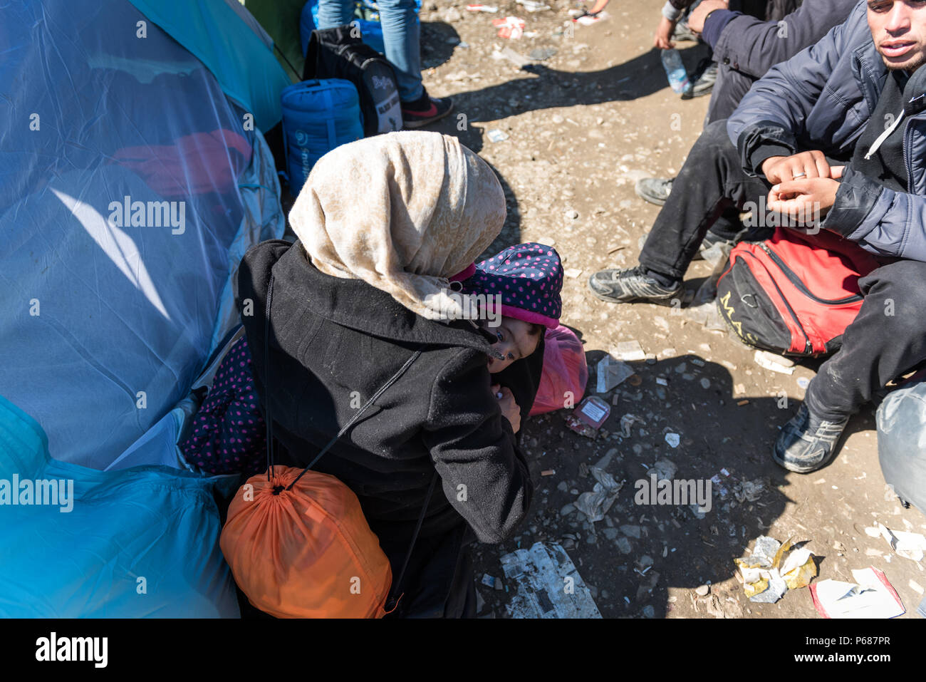 A refugee mother holds her child as she waits close to the border gate ...