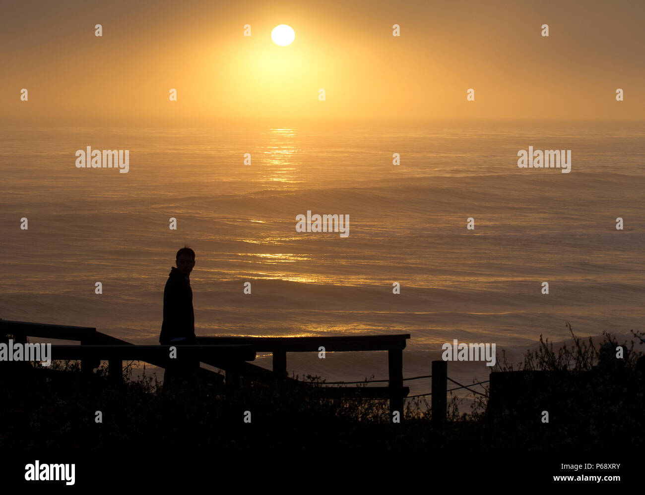 Silhouetted man watching sun setting through fog over pacific hi-res ...
