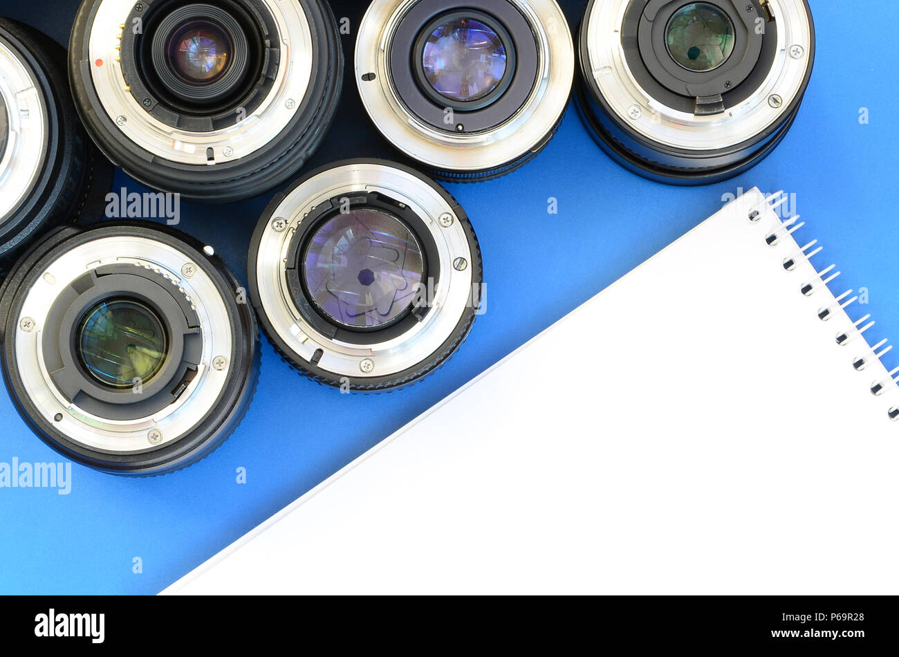Several photographic lenses and white notebook lie on a bright blue ...