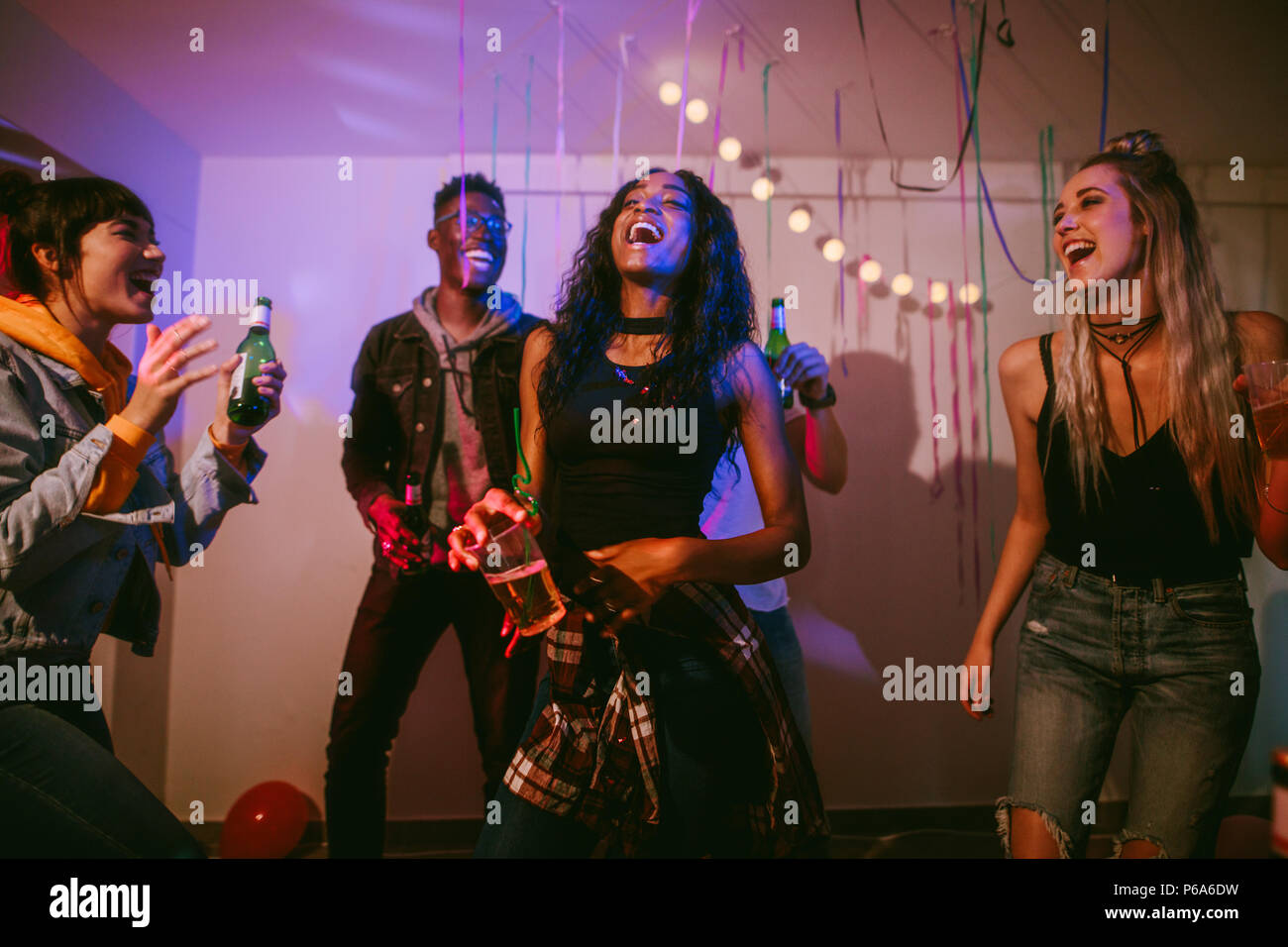 Friends laughing and dancing holding drinks at house party. Young women ...
