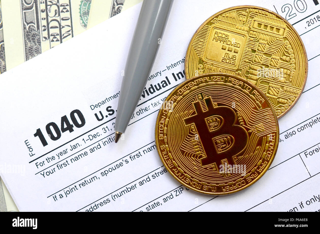 The pen, bitcoins and dollar bills is lies on the tax form 1040 U.S ...