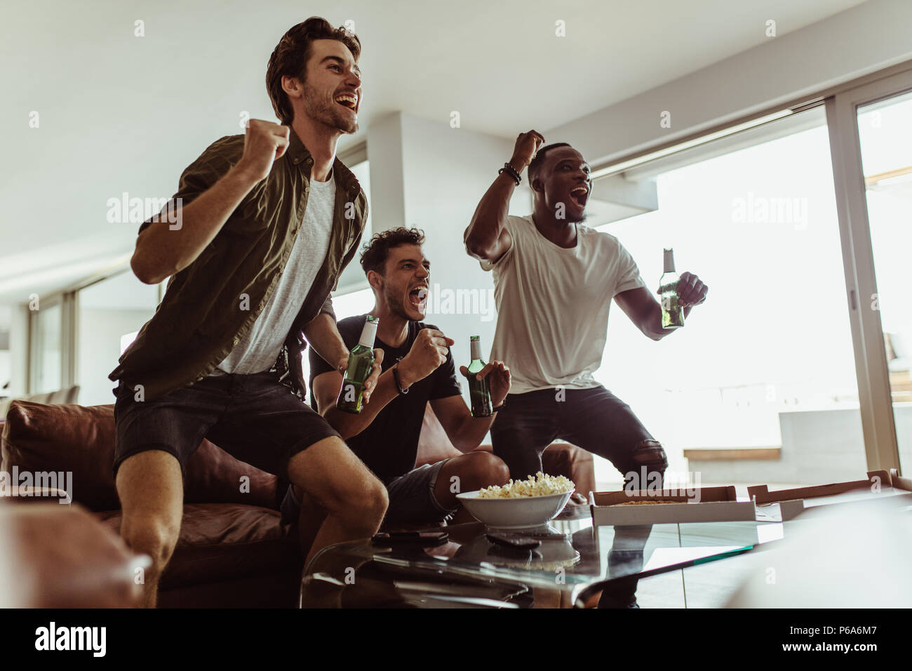 Three friends jumping in excitement holding beer bottles while watching ...