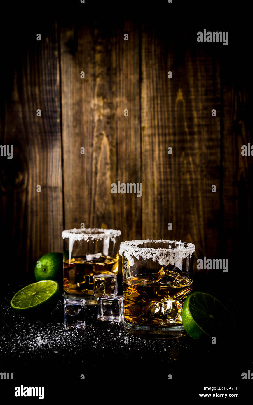 Two tequila shot glasses on dark background, with ice cubes, salt and ...
