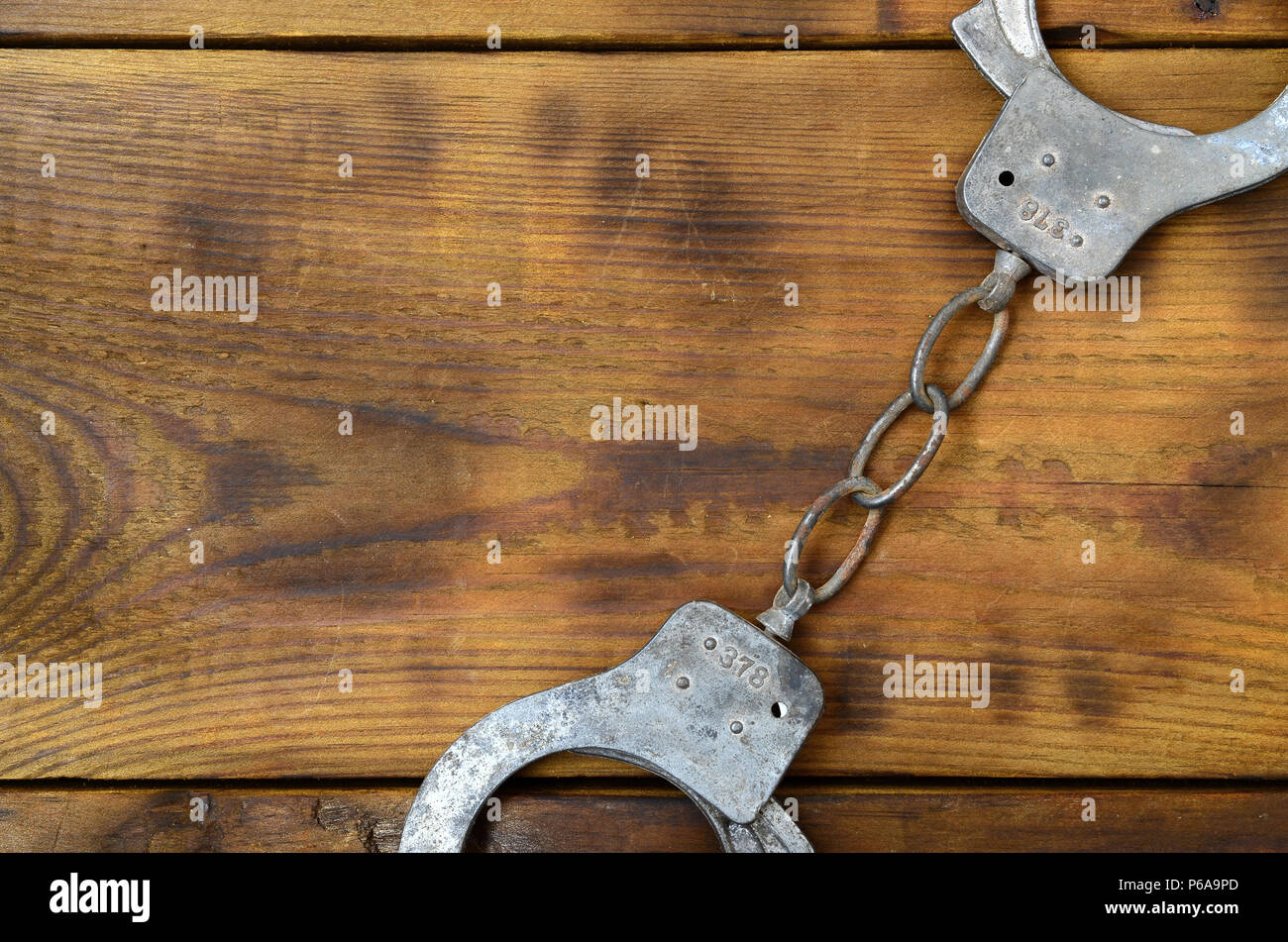Old and rusty police handcuffs lie on a scratched wooden surface. The ...