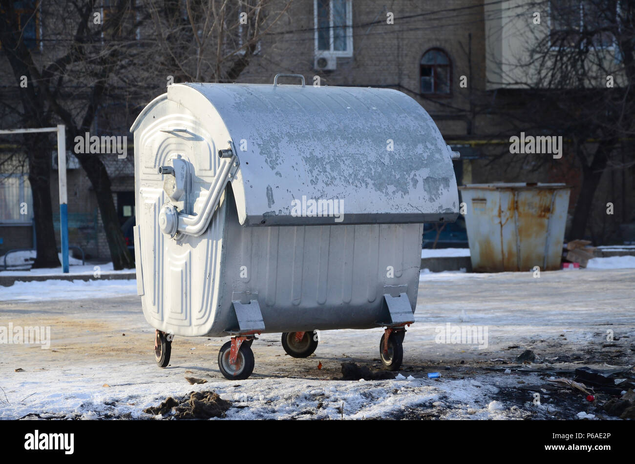 A silver garbage container stands near residential buildings in winter ...