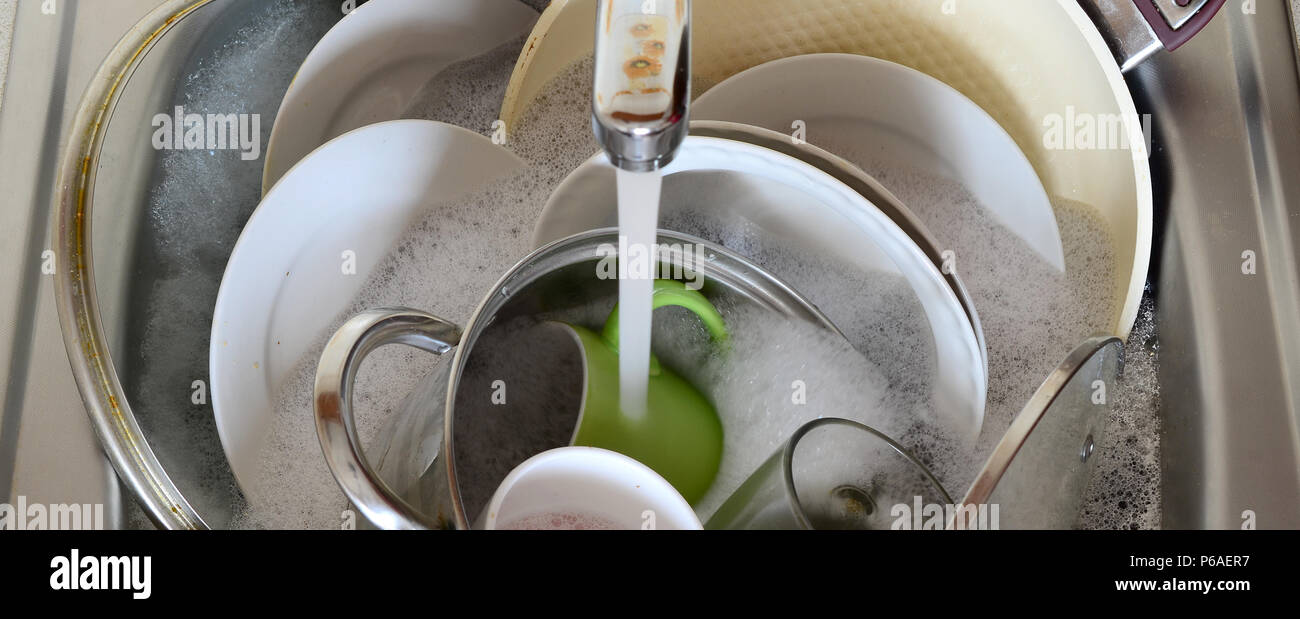 Dirty dishes and unwashed kitchen appliances lie in foam water under a ...