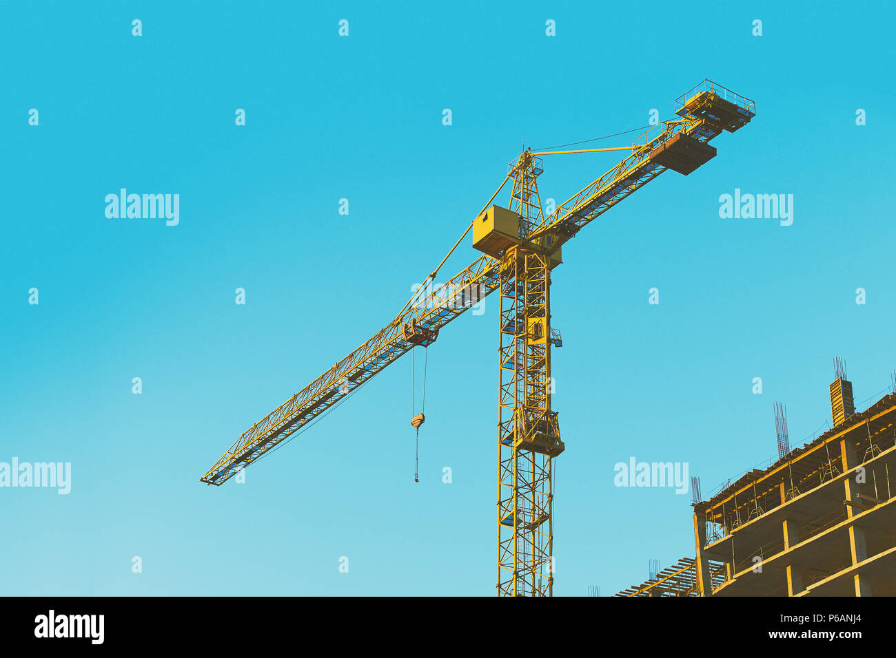 Yellow tower crane at construction site on blue sky background toned ...