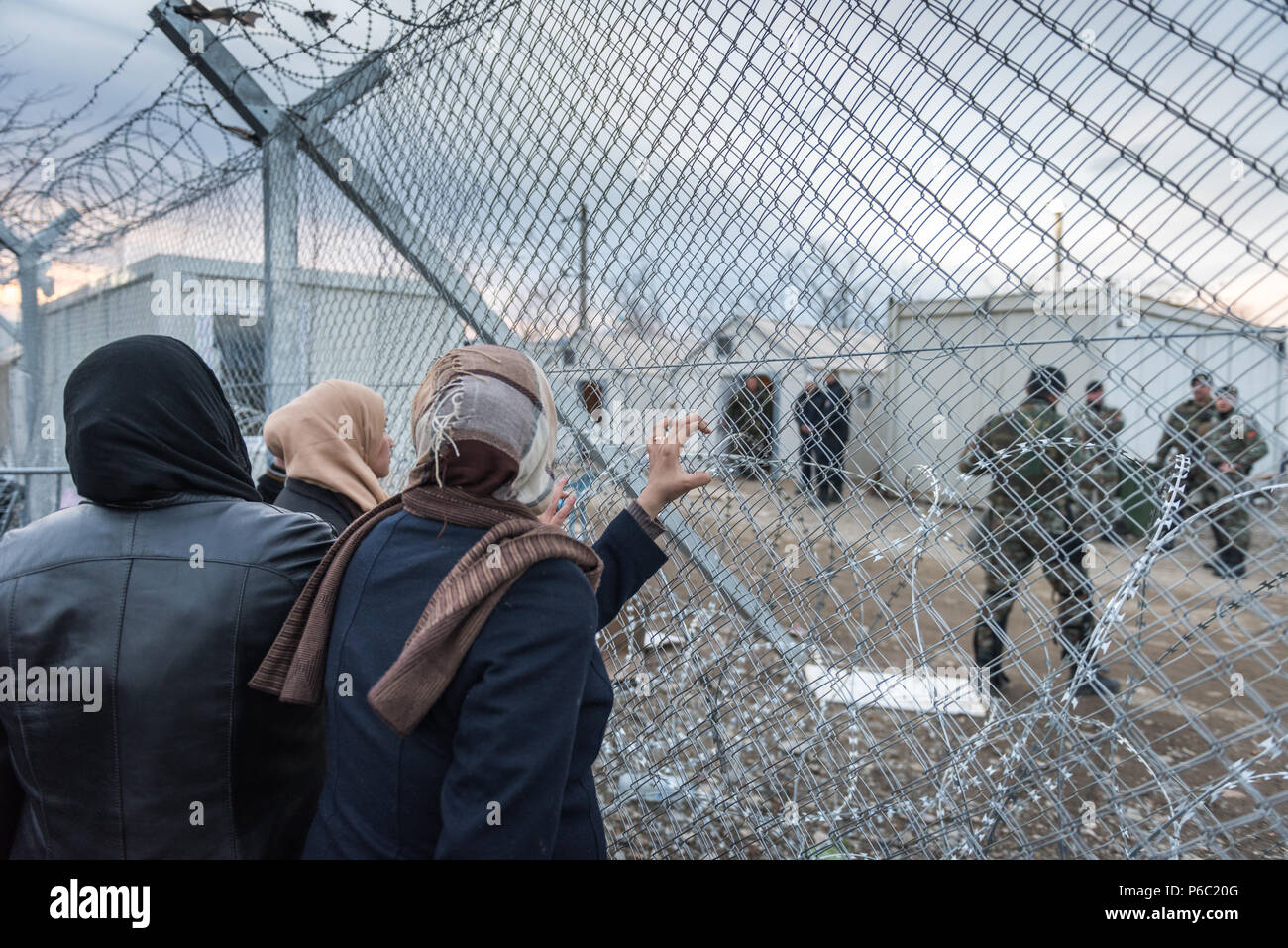 women look through barbed wire when migrants and refugees wait to cross ...