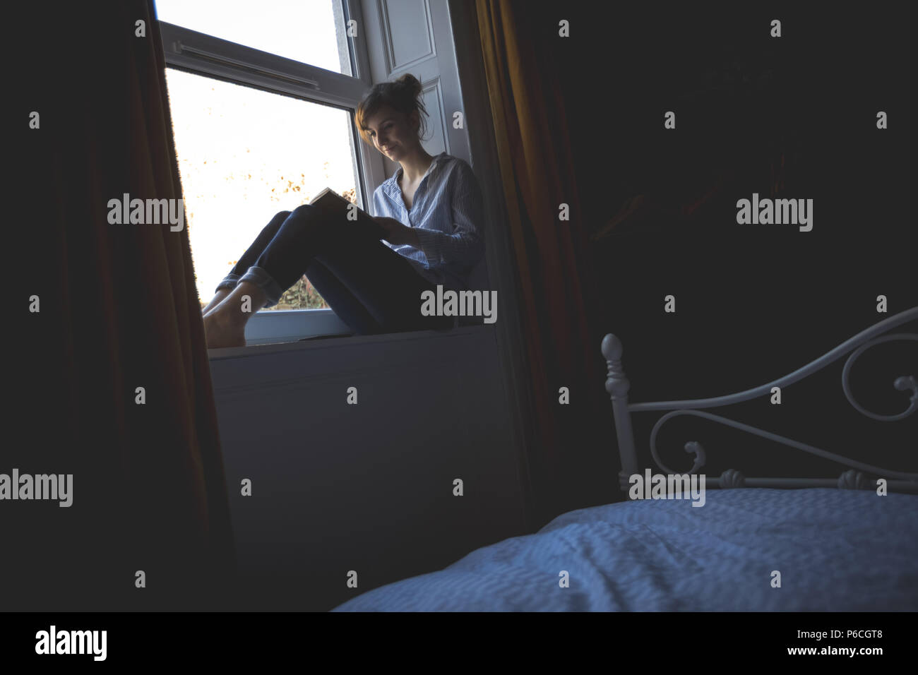 Woman reading book on window sill Stock Photo - Alamy