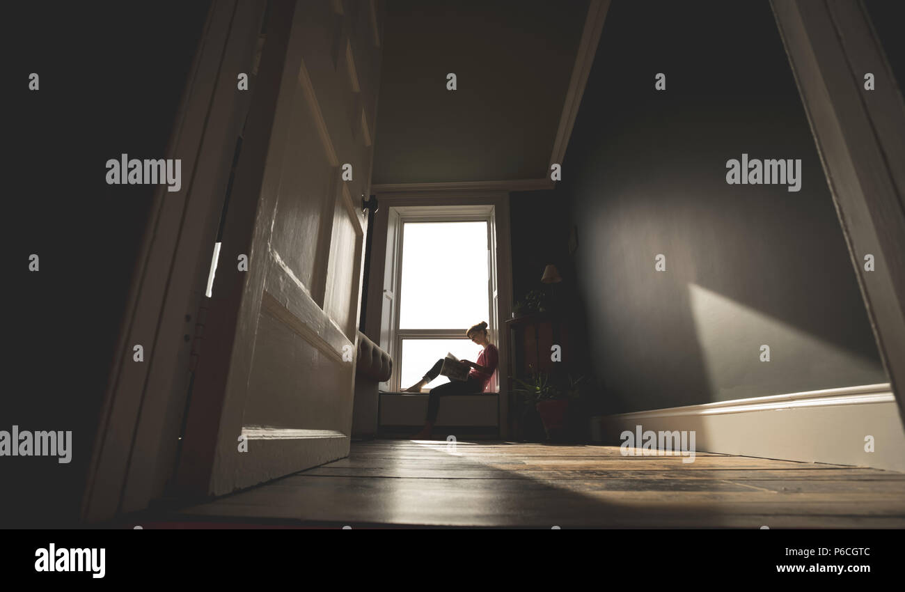 Woman reading book on window sill Stock Photo - Alamy