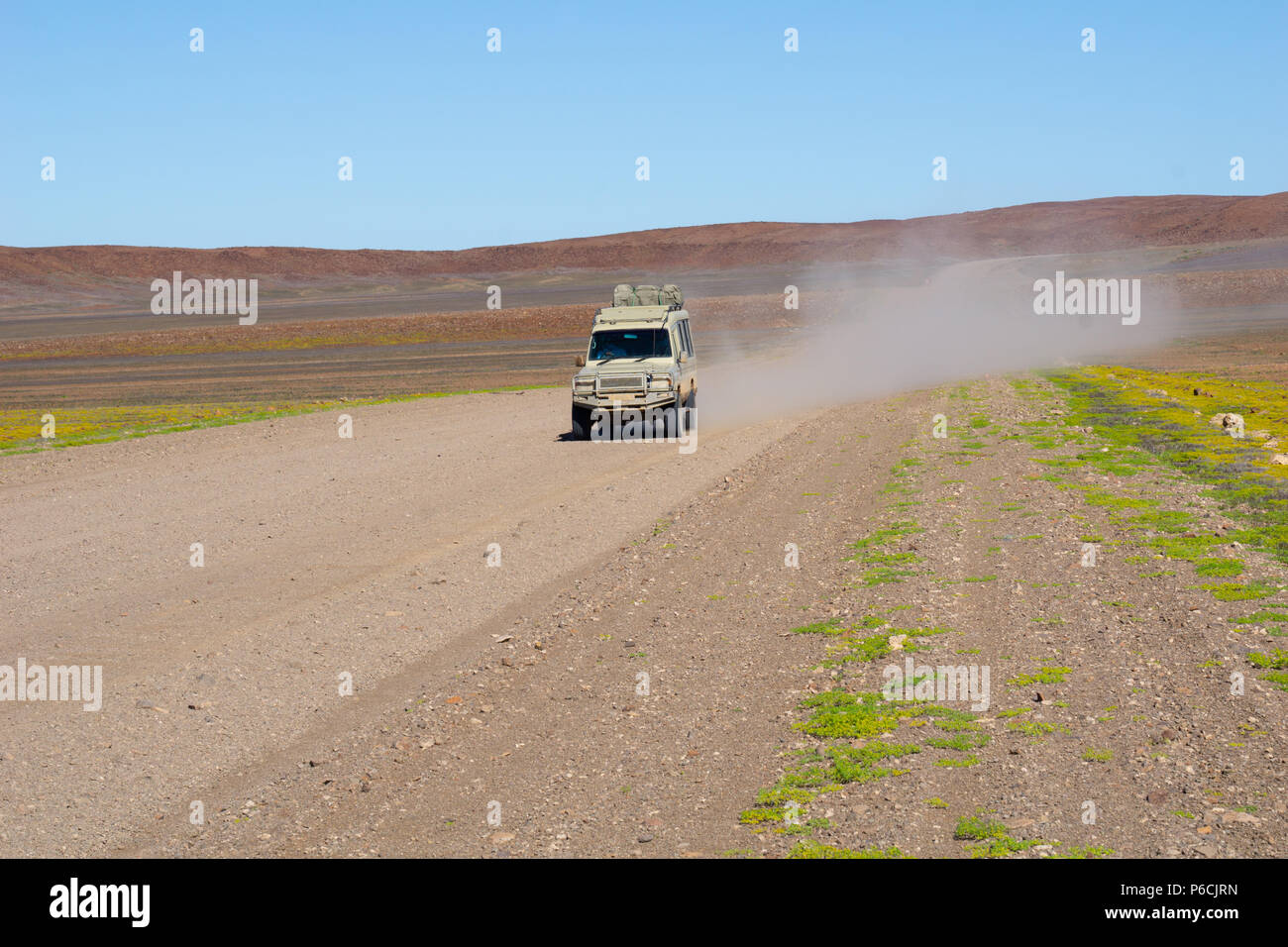 Dust trail follows safari vehicle along dusty road through Namibian ...