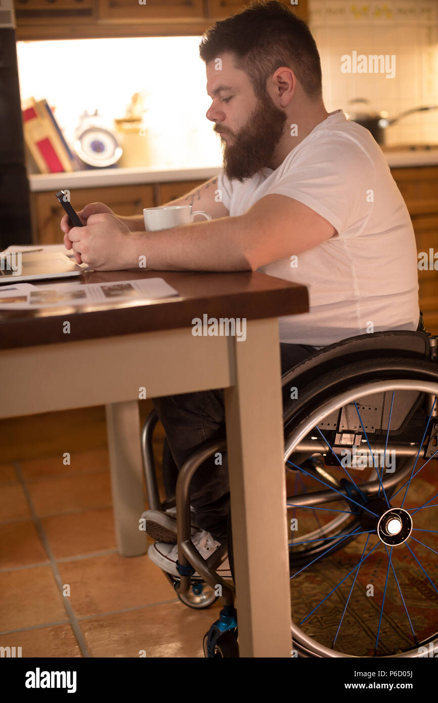 Disabled man using mobile phone while working on laptop Stock Photo - Alamy