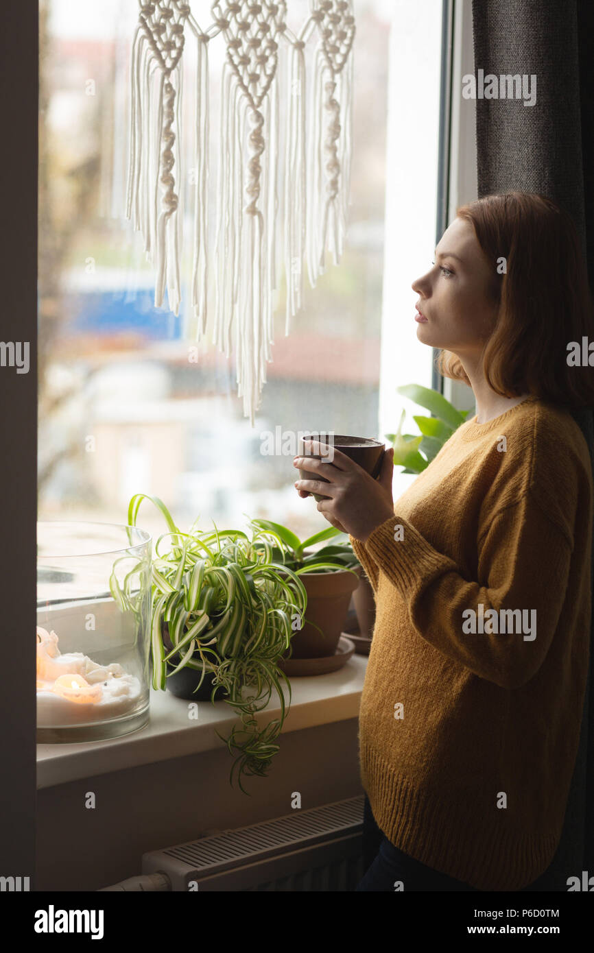 Woman having coffee while looking through window Stock Photo - Alamy