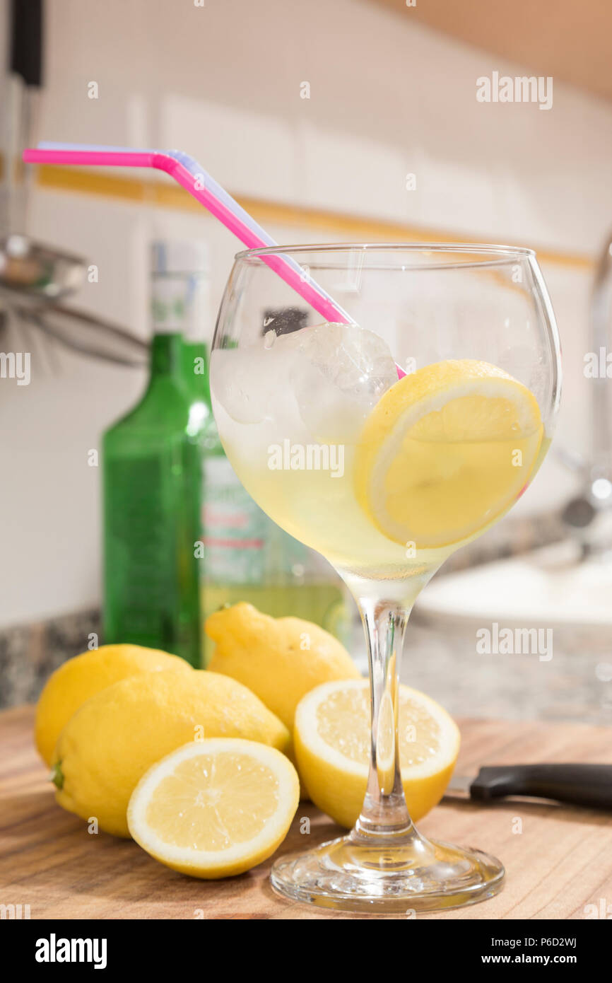 glass with slice of lemon, lemons behind and bottles. Preparation in ...