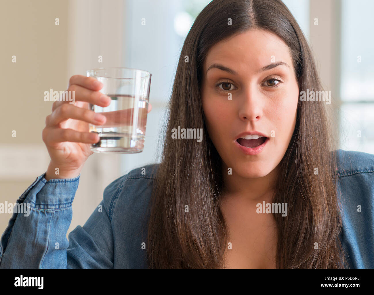Young woman drinking glass of water at home scared in shock with a ...