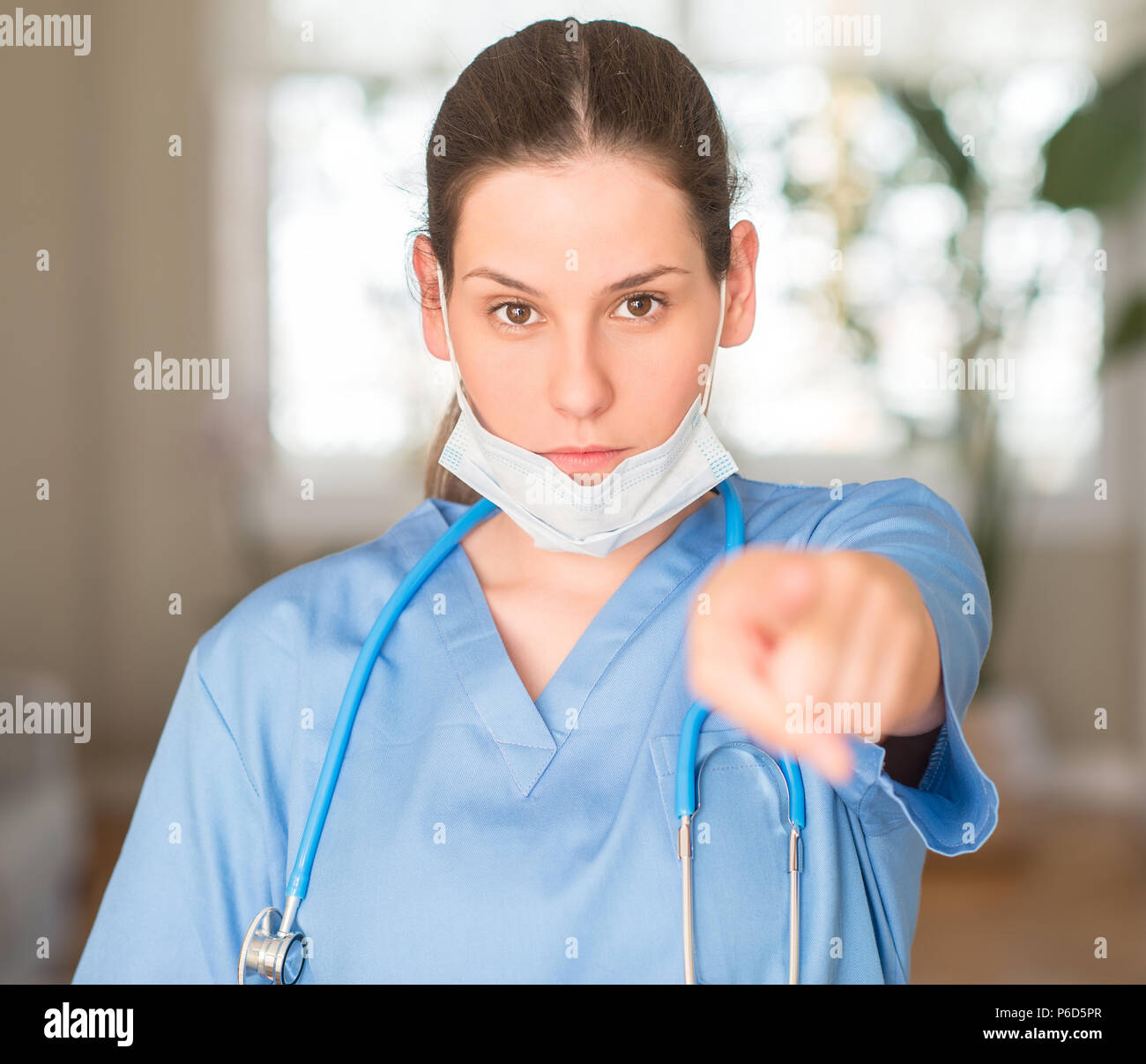 Young nurse woman wearing mask and stethoscope pointing with finger to ...