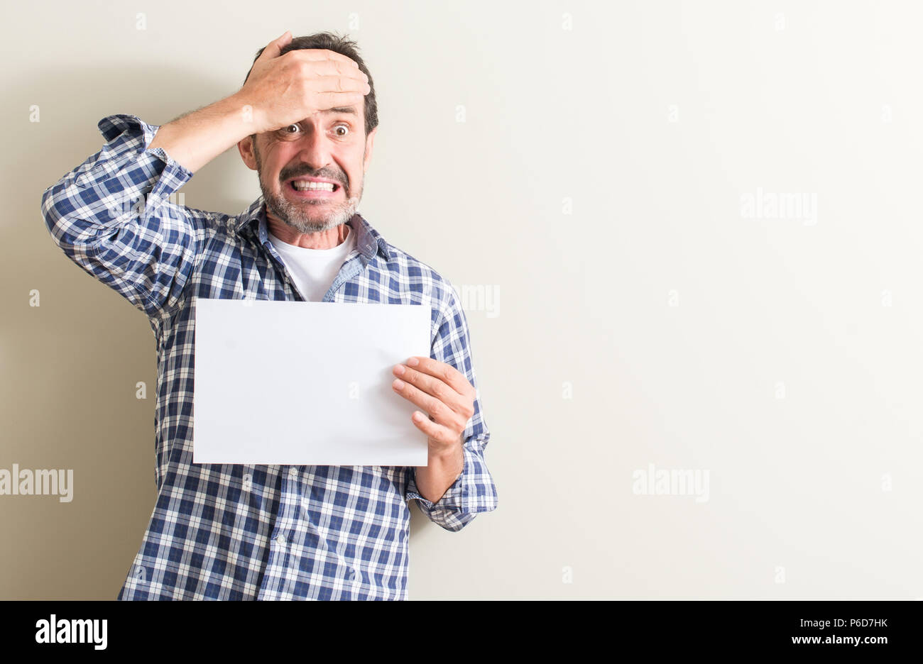 Senior man holding blank paper sheet stressed with hand on head ...