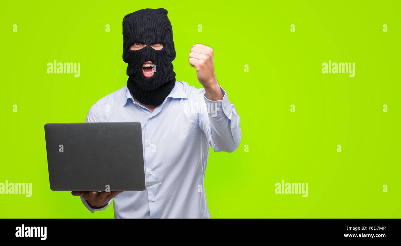 Business hacker man holding a computer laptop annoyed and frustrated ...
