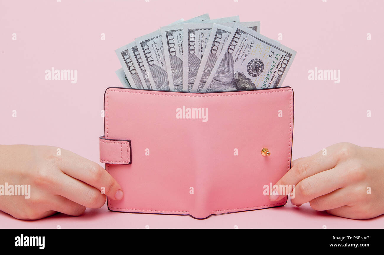 Dollars and pink wallet in woman's hand on a pink background with copy ...