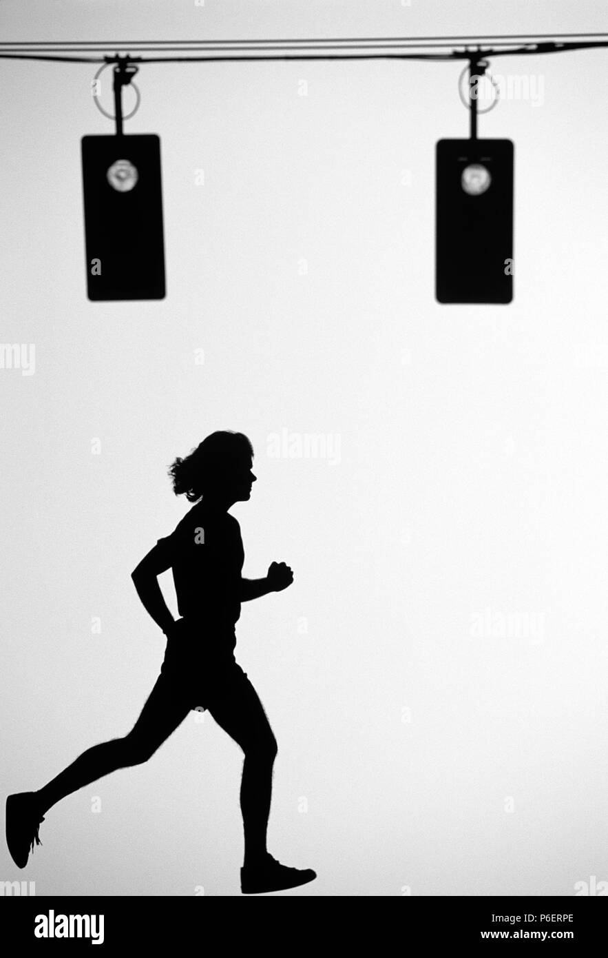Runner crossing street with red traffic lights silhouetted at sunset ...