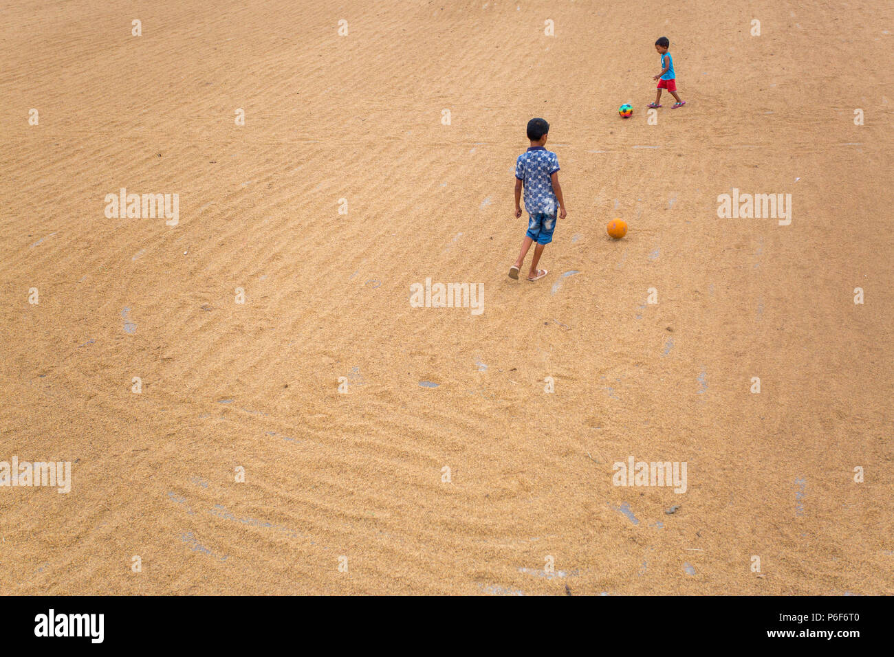 Some of the children are playing football on dry paddy in the sun at ...